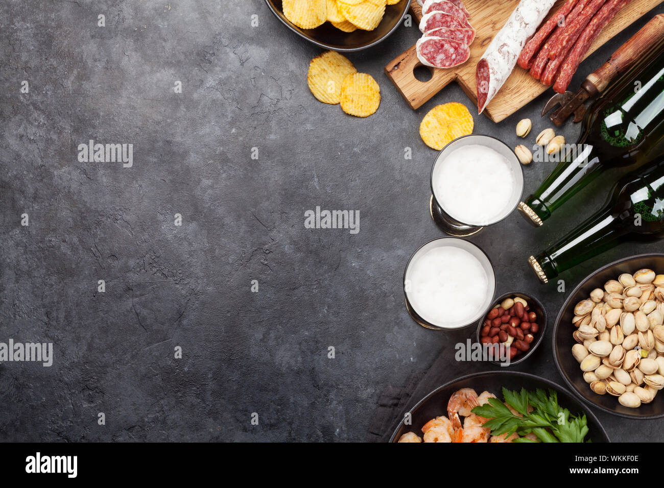 Draft beer and snacks on stone background. Nuts, chips, sausages and ...