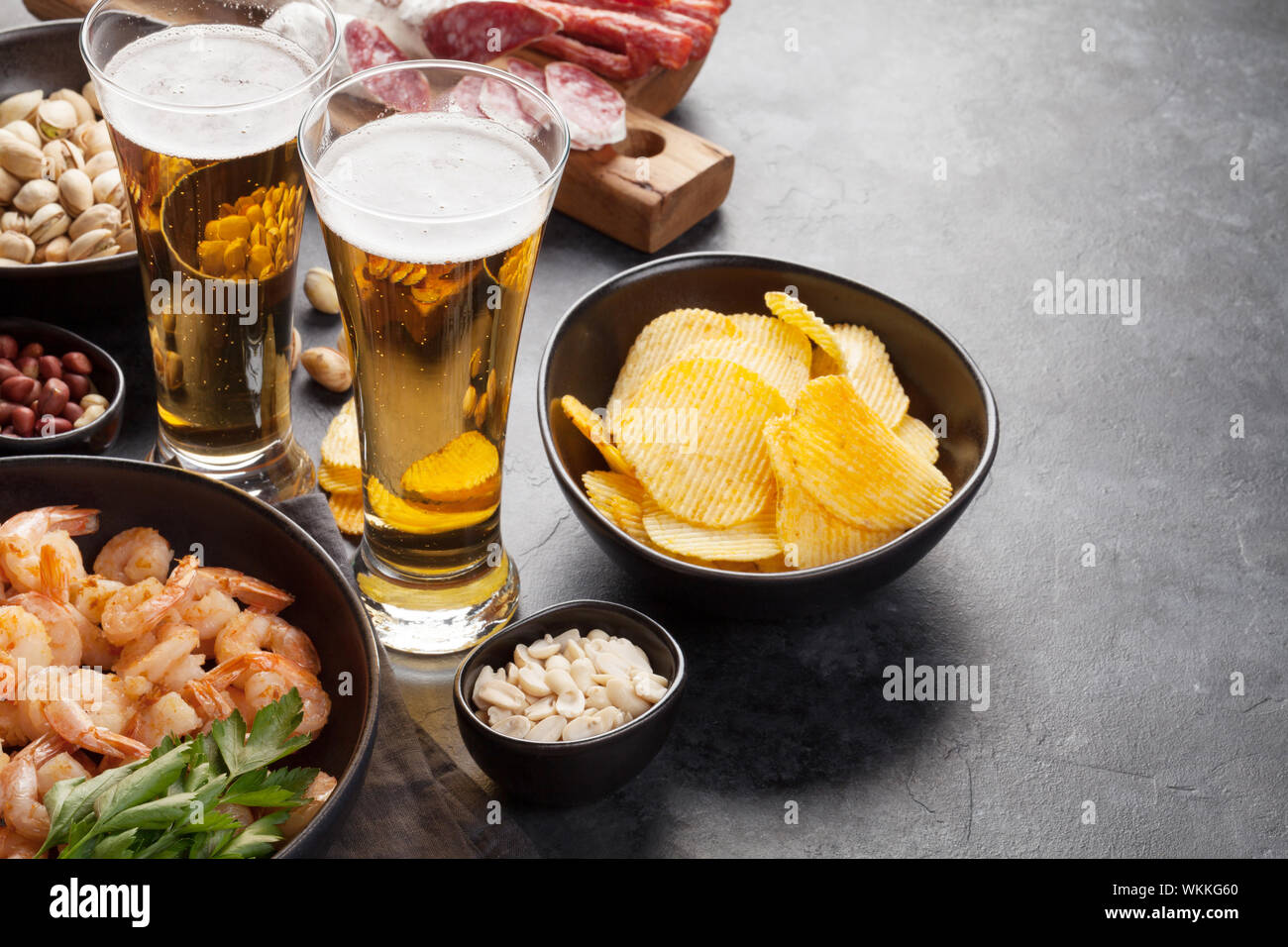 Draft beer and snacks on stone background. Nuts, chips, sausages and ...