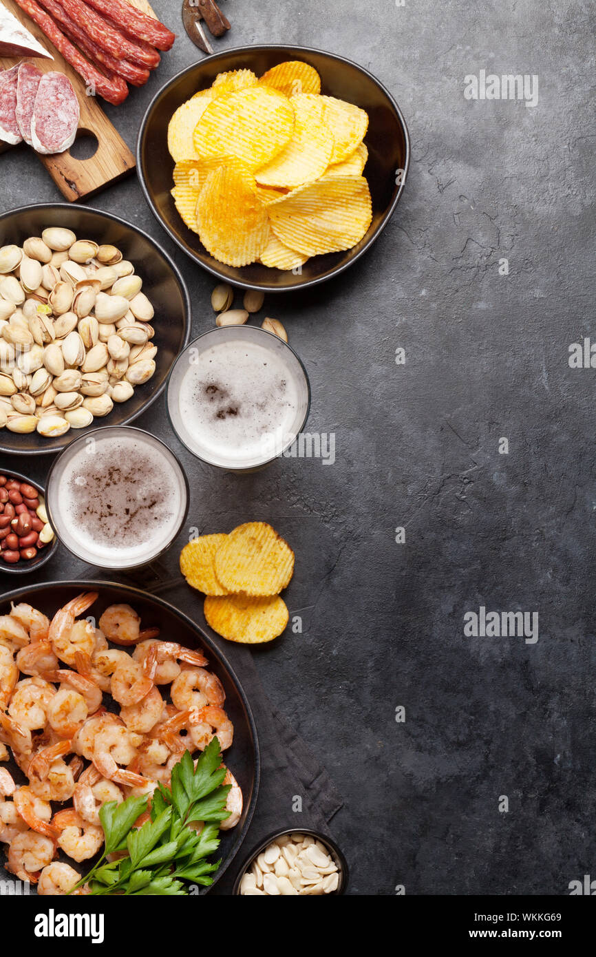 Draft beer and snacks on stone background. Nuts, chips, sausages and ...