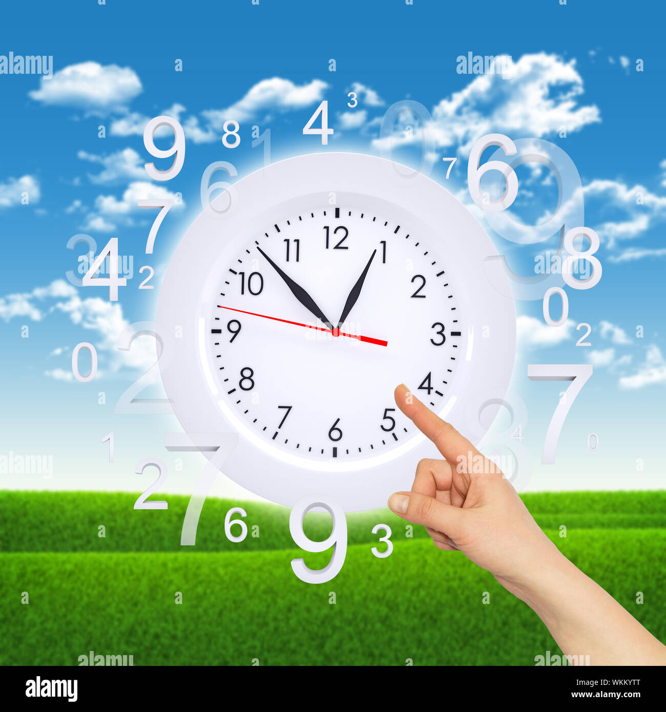 Finger points to clock face with figures on background of green grass ...