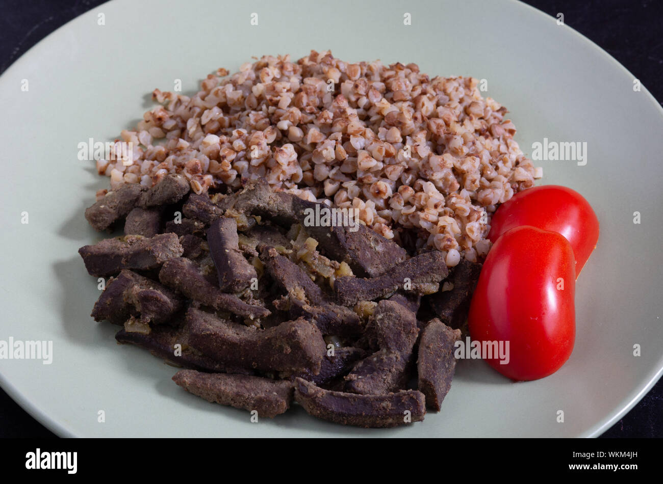 Cooked liver and buckwheat on light green plate on the black background ...