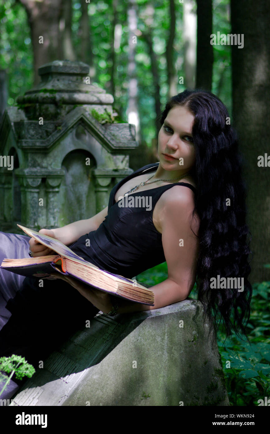 Gothic girl with old book posing on gravestone Stock Photo - Alamy