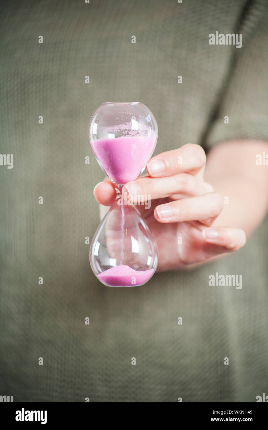 pink sand clock in woman hands over green background Stock Photo - Alamy