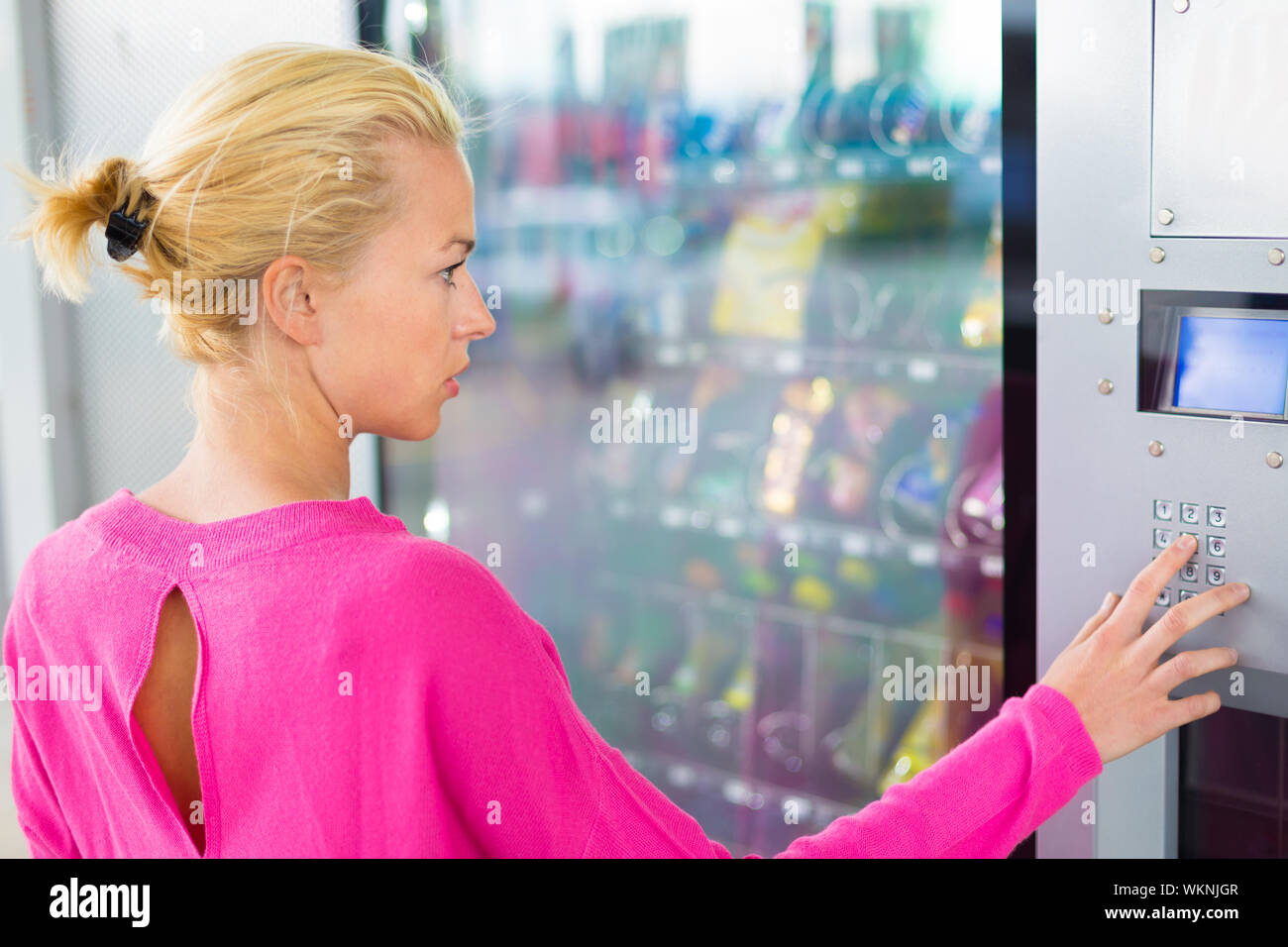 Caucasian woman wearing pink top using a coin operated modern vending ...