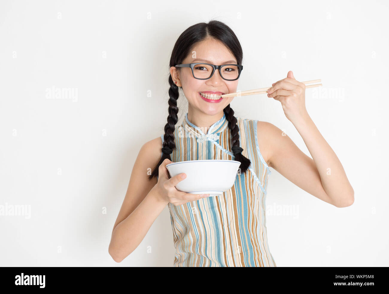 Portrait of Asian Chinese female eating, using chopsticks holding rice ...