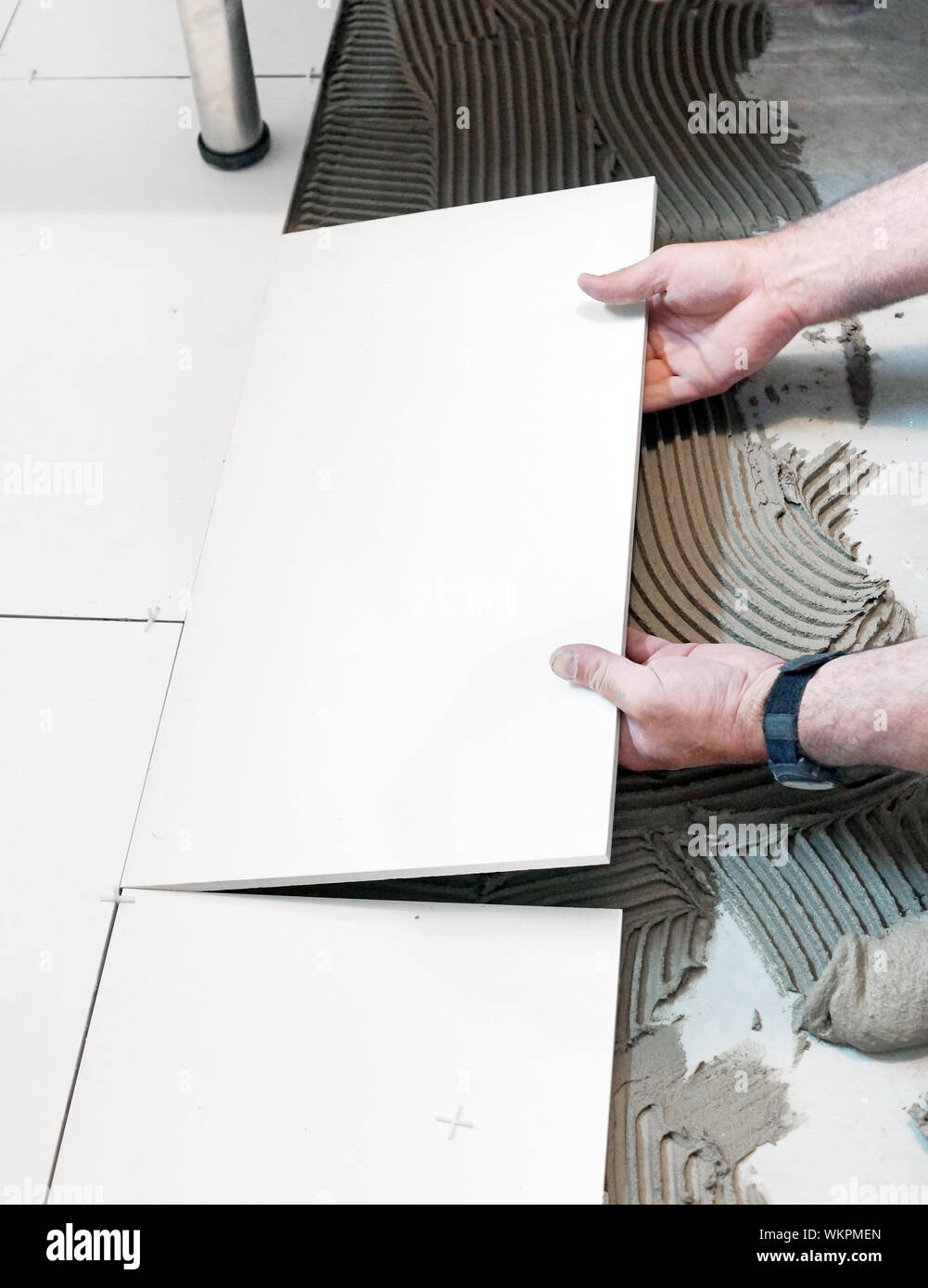 Worker laying down white ceramic or procelain tiles on the floor, house ...
