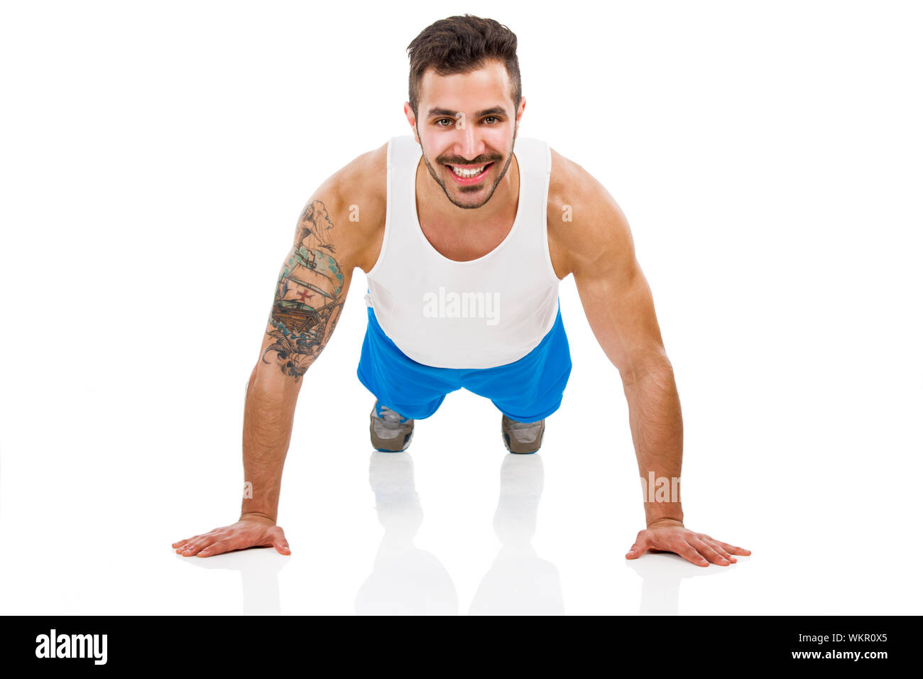 Athletic young man smiling and making pushups, isolated over a white ...