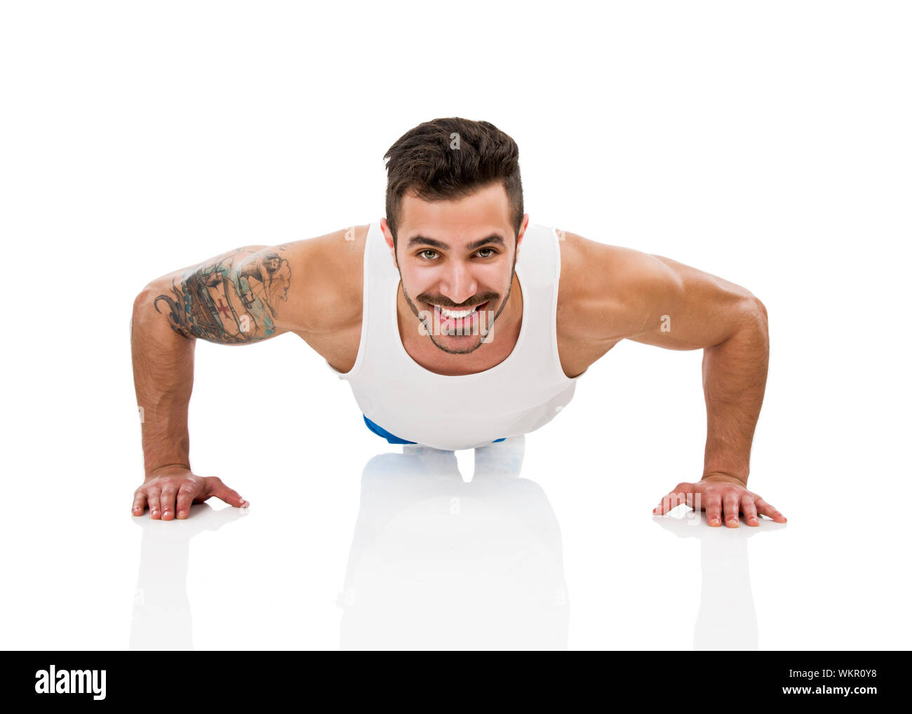 Athletic young man smiling and making pushups, isolated over a white ...