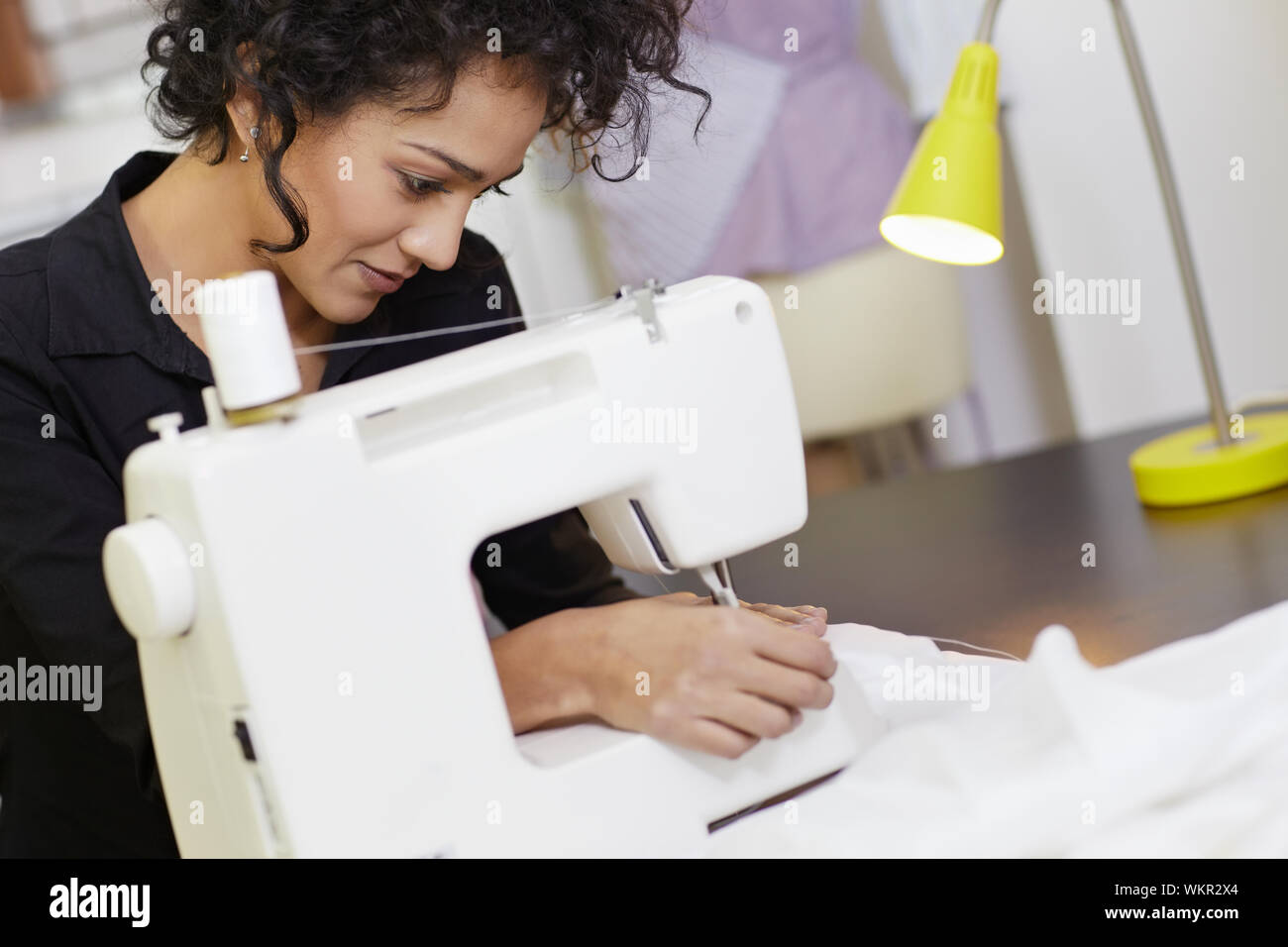 Young hispanic female dressmaker using sewing machine. Horizontal shape ...