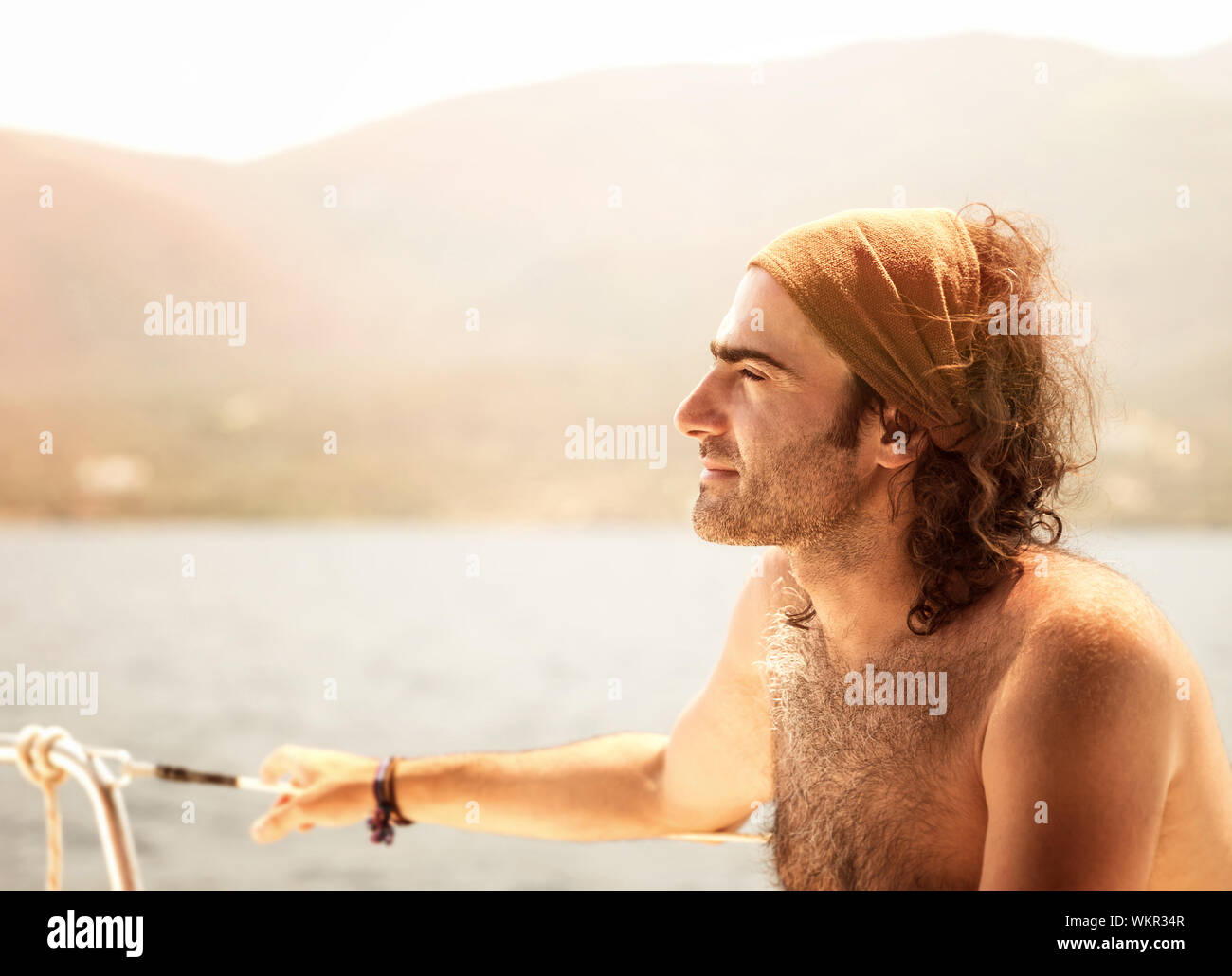 Portrait of man sitting on sail boat and enjoying mild sunset light ...