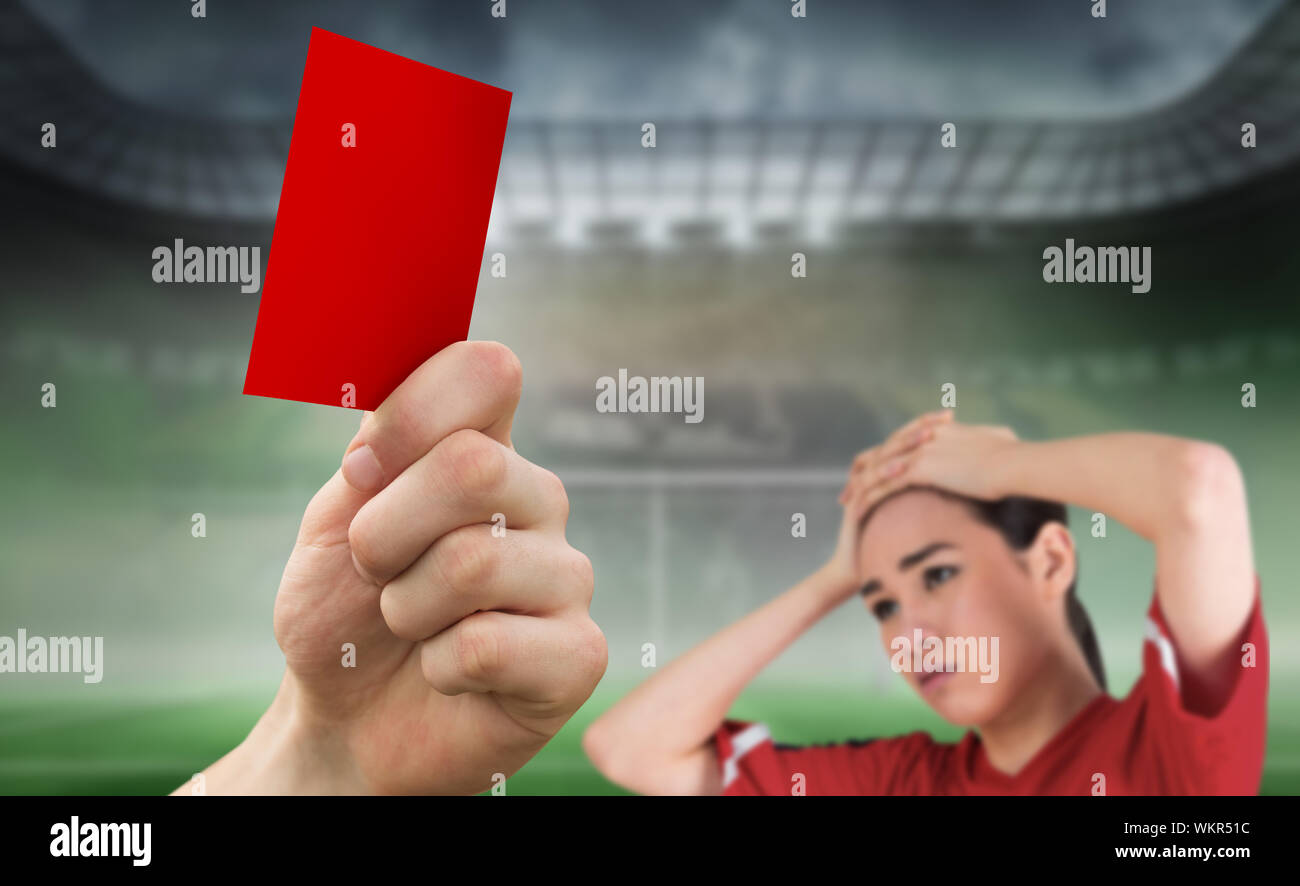 Hand holding up red card against football pitch in large stadium with ...