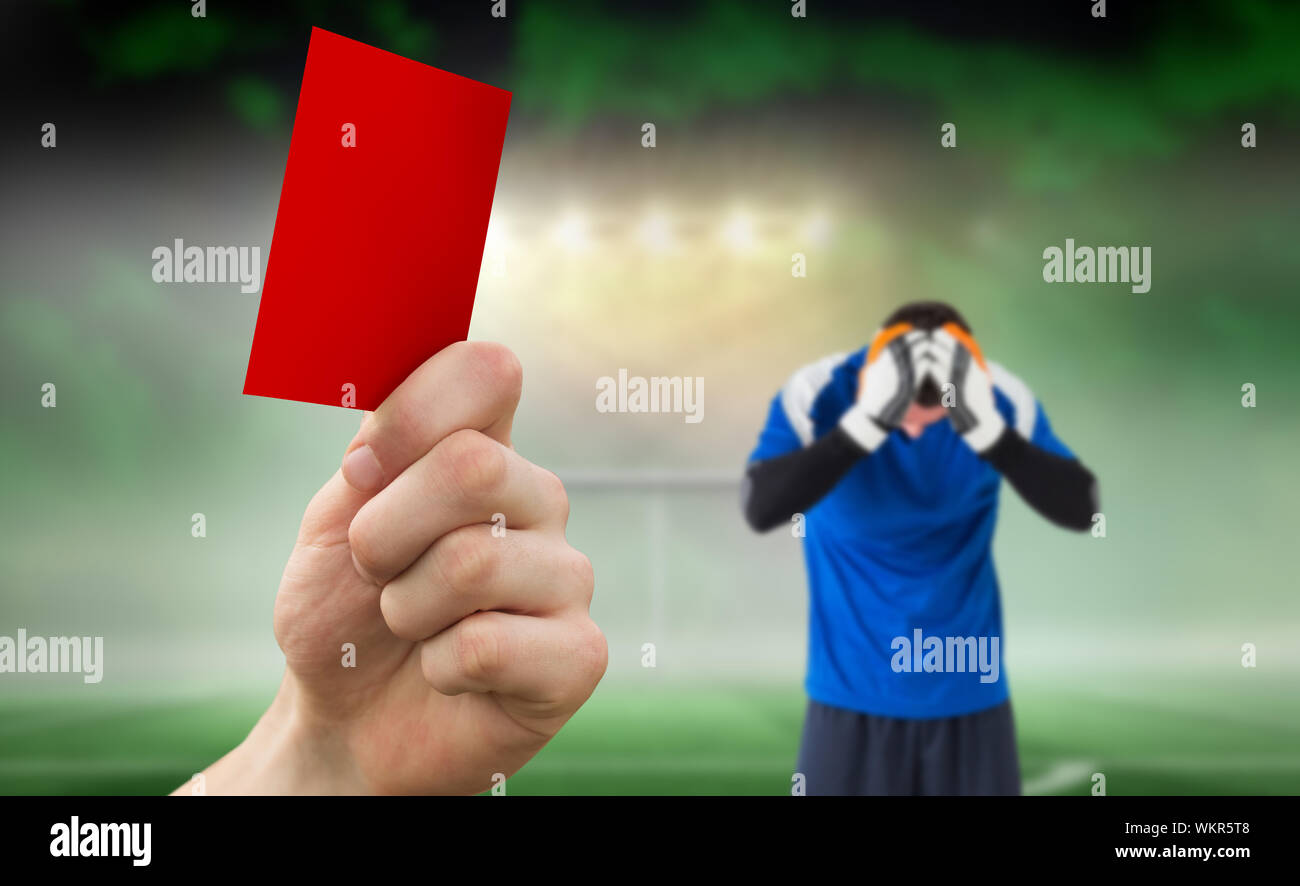 Hand holding up red card against football pitch under spotlights with ...