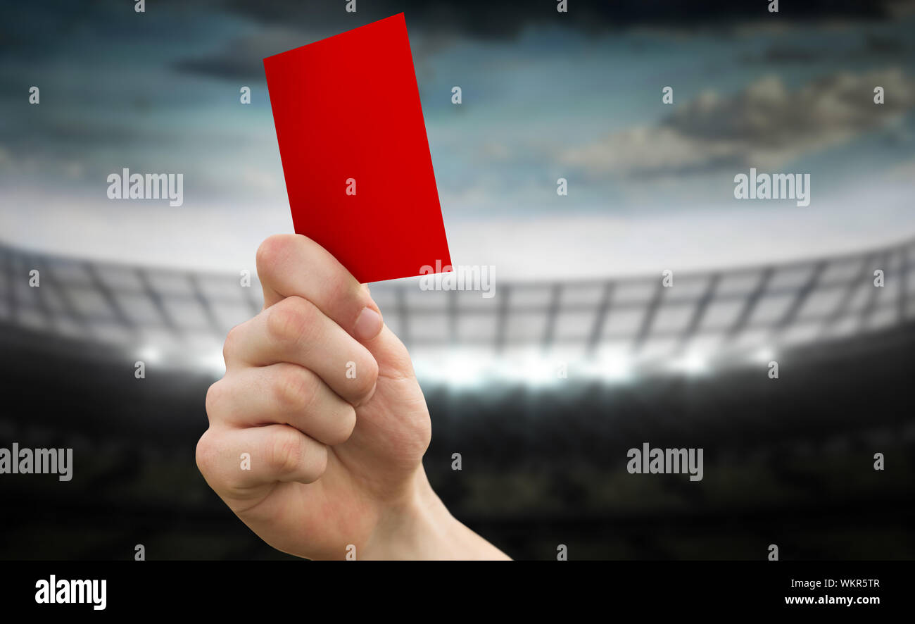 Hand holding up red card against large football stadium under cloudy ...
