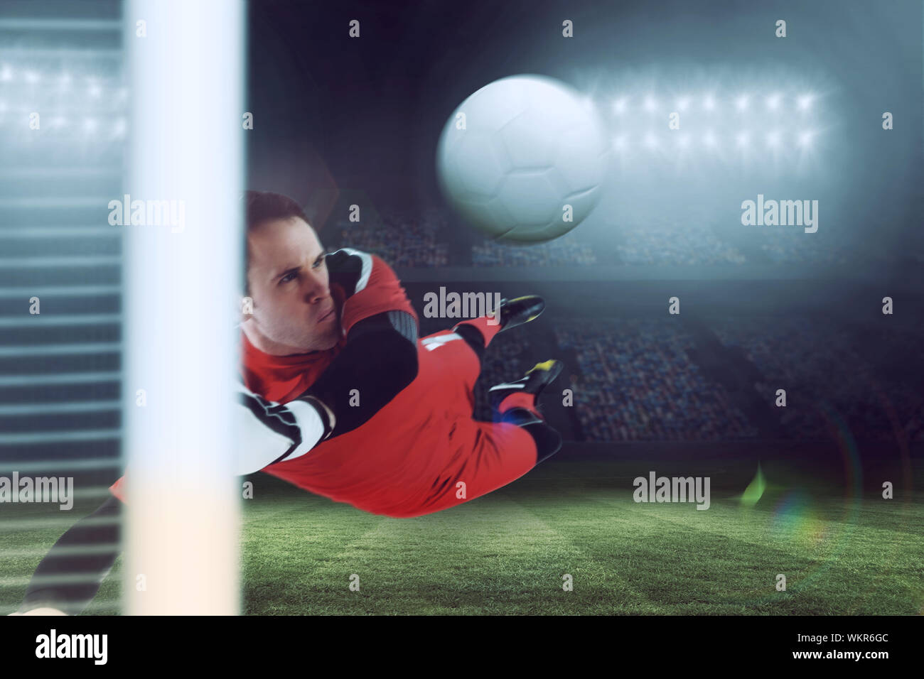 Fit goal keeper jumping up against large football stadium under blue ...
