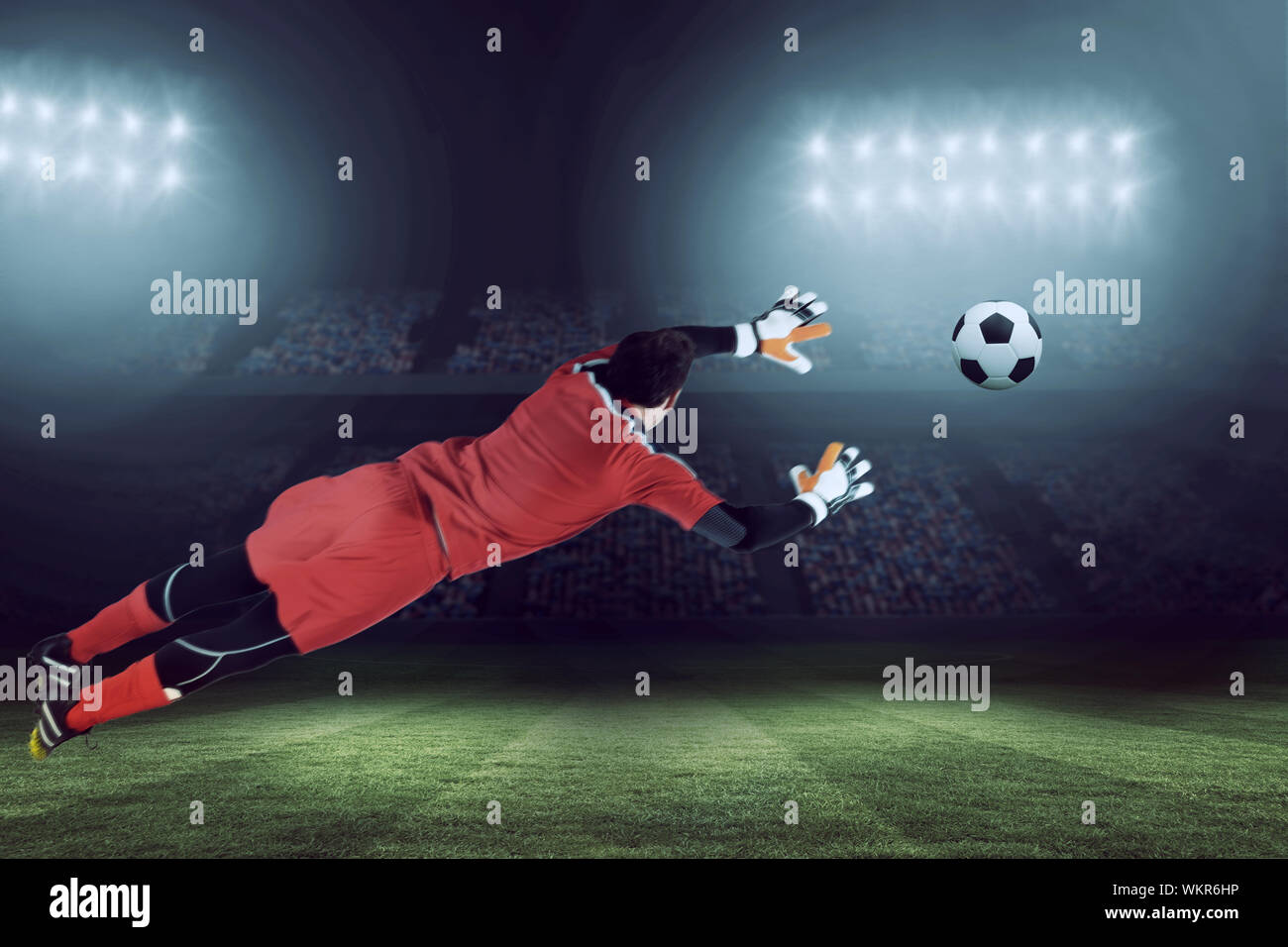 Fit goal keeper jumping up against large football stadium under blue ...