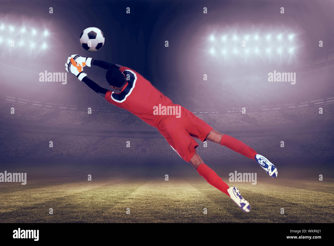 Goalkeeper in red making a save against large football stadium under ...