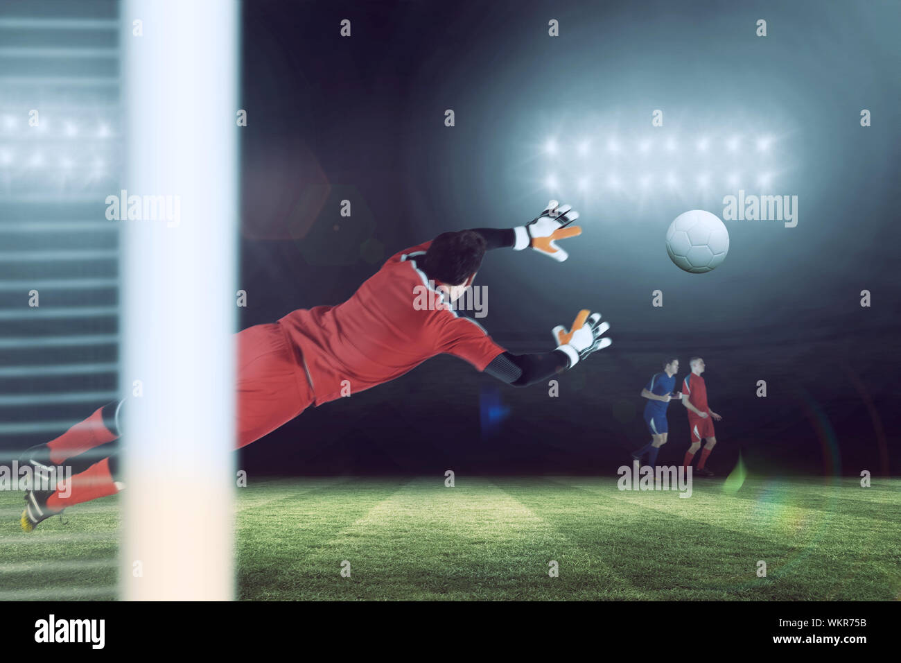 Fit goal keeper jumping up against football pitch under spotlights ...