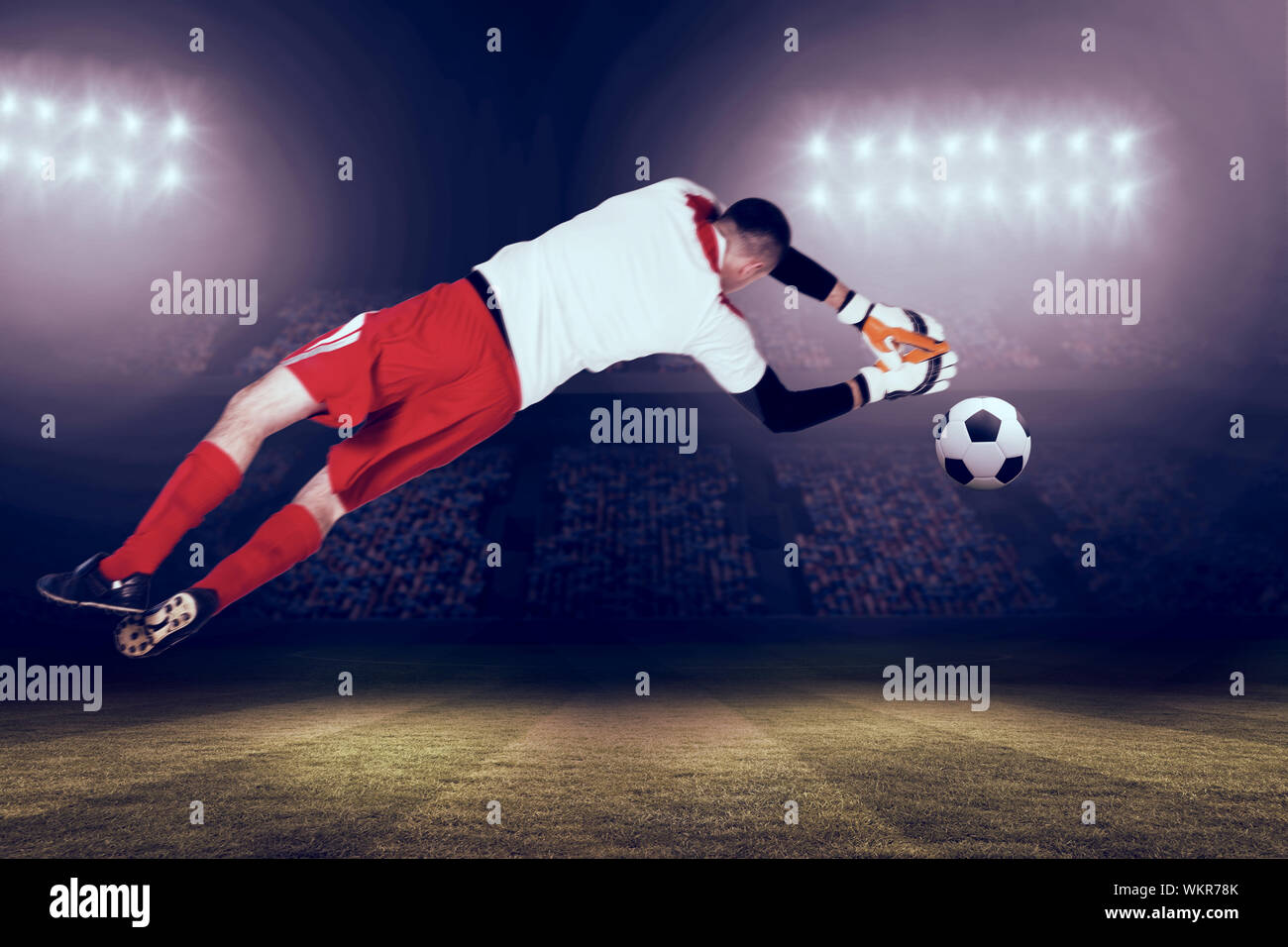 Fit goal keeper jumping up against large football stadium under blue ...