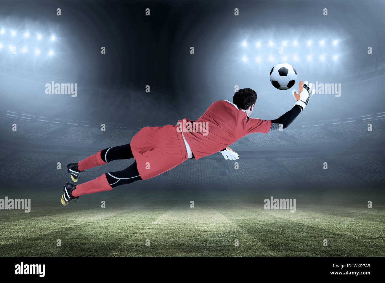 Fit goal keeper jumping up against large football stadium under blue ...