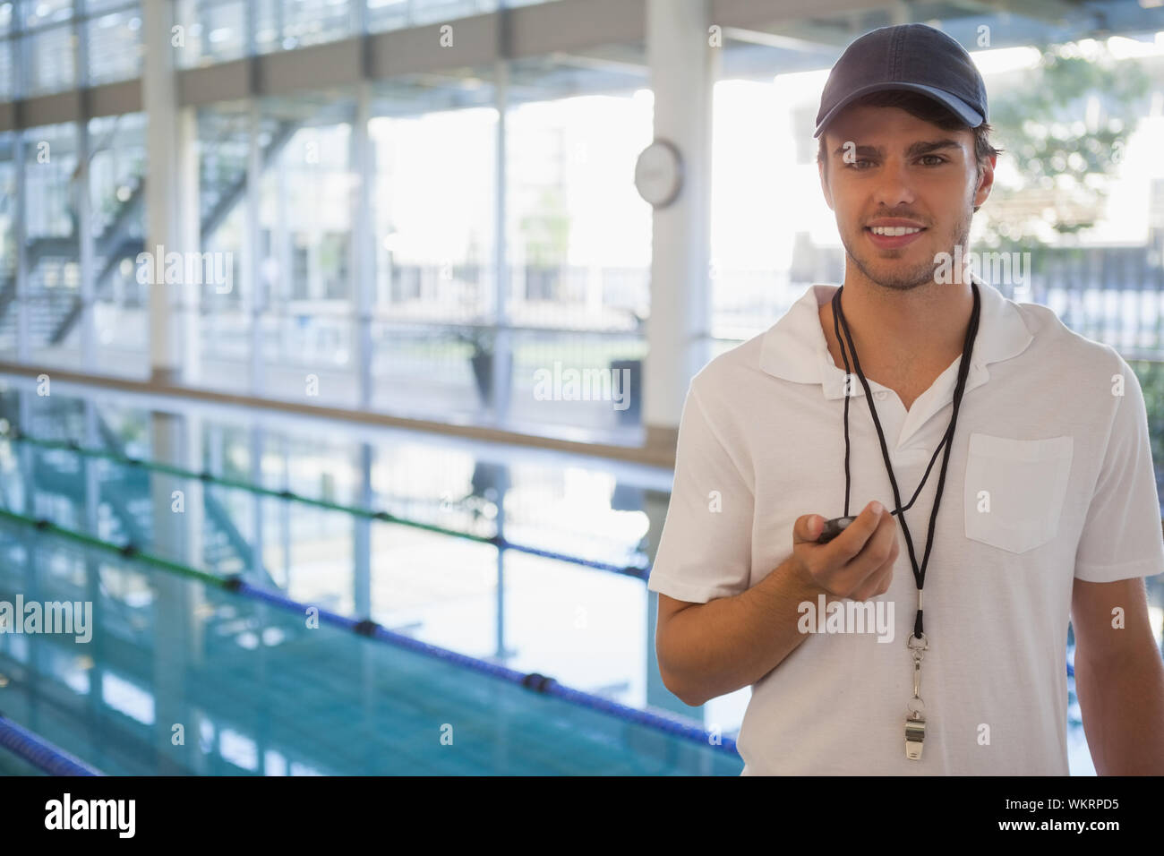 Swimming coach standing by the pool smiling at camera at the leisure ...
