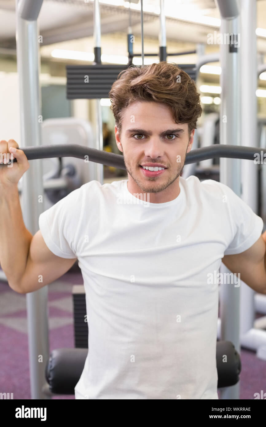 Fit man using weights machine for arms smiling at camera at the gym ...
