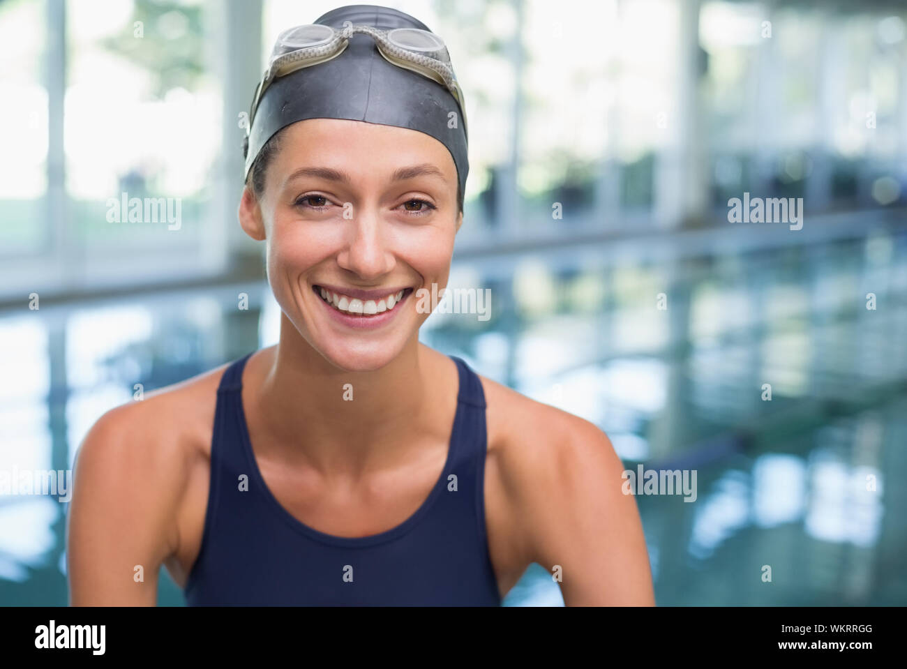 Pretty swimmer smiling at camera by the pool at the leisure center ...