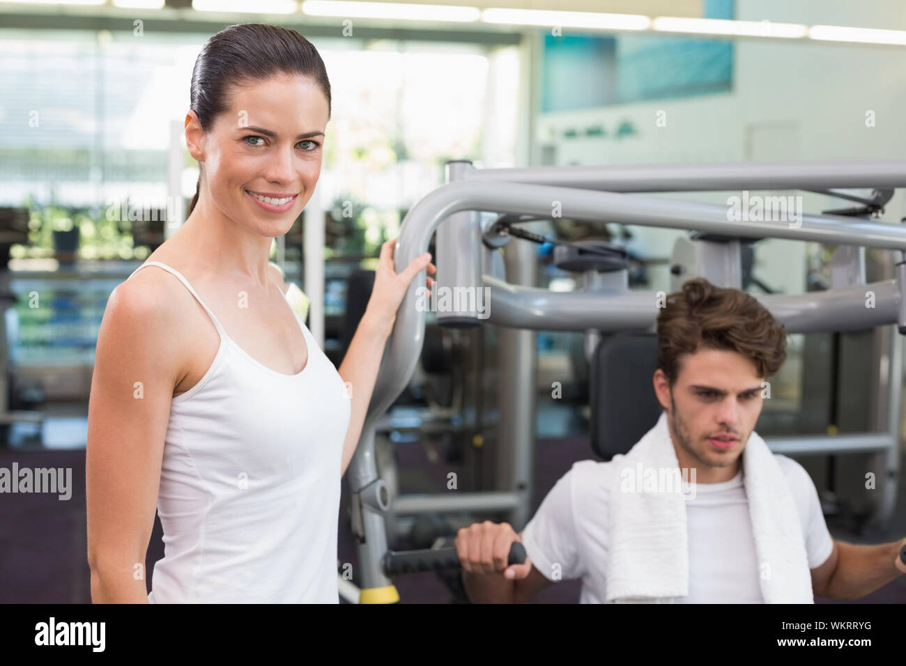Fit man using weights machine with trainer smiling at camera at the gym ...