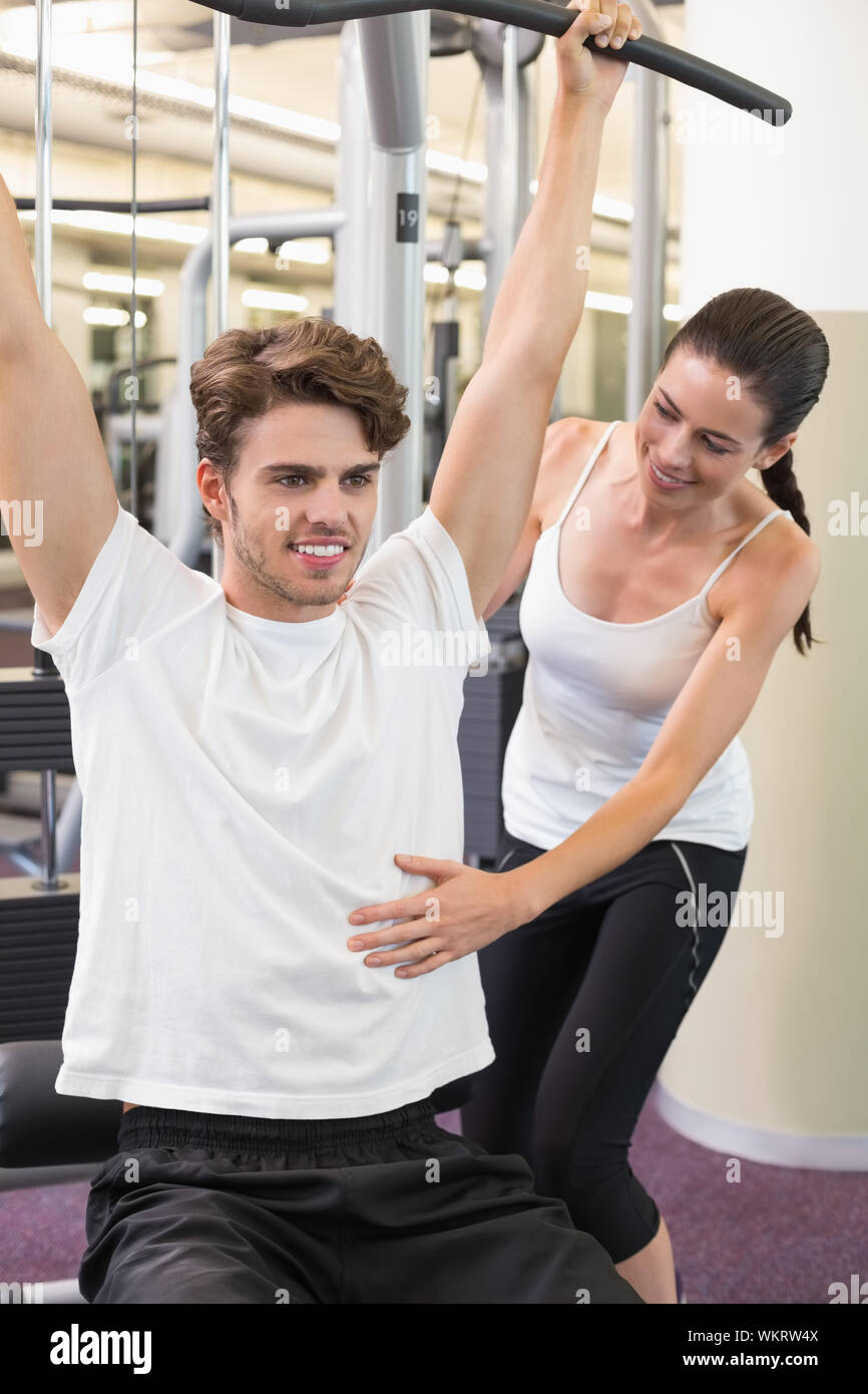 Fit man using weights machine for arms with his trainer at the gym ...