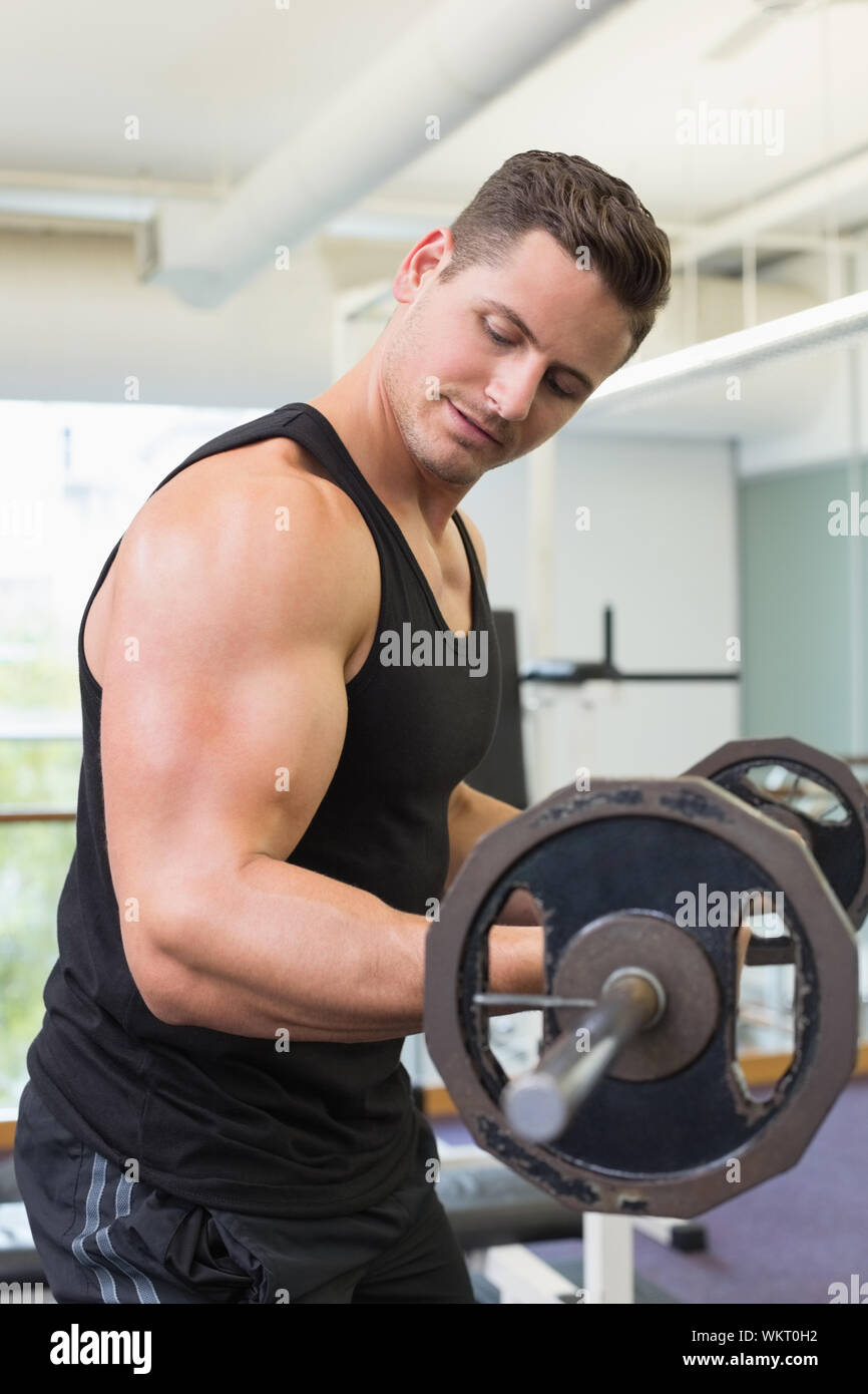 Muscular bodybuilder lifting heavy black barbell weight at the gym ...