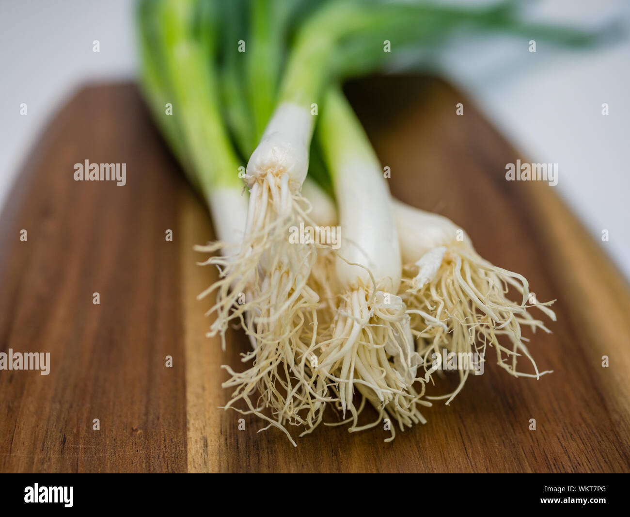 Close-up of bunch of spring onions laying on brown wooden board ...