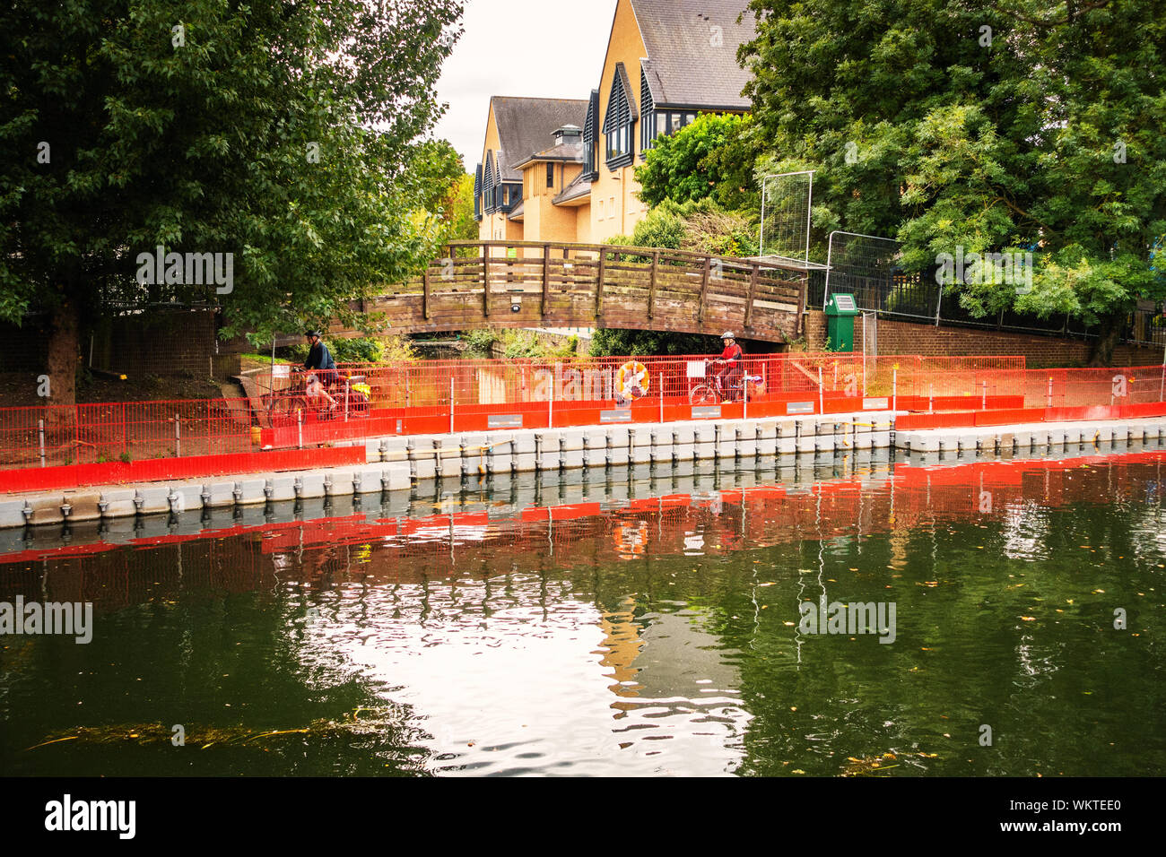 2 cyclists ride over a temporary floating river footpath bridge next to ...