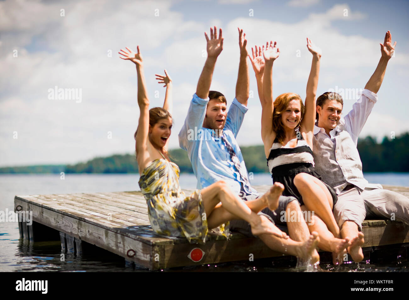 Group of friends sitting on a jetty, splashing in the lake with their ...