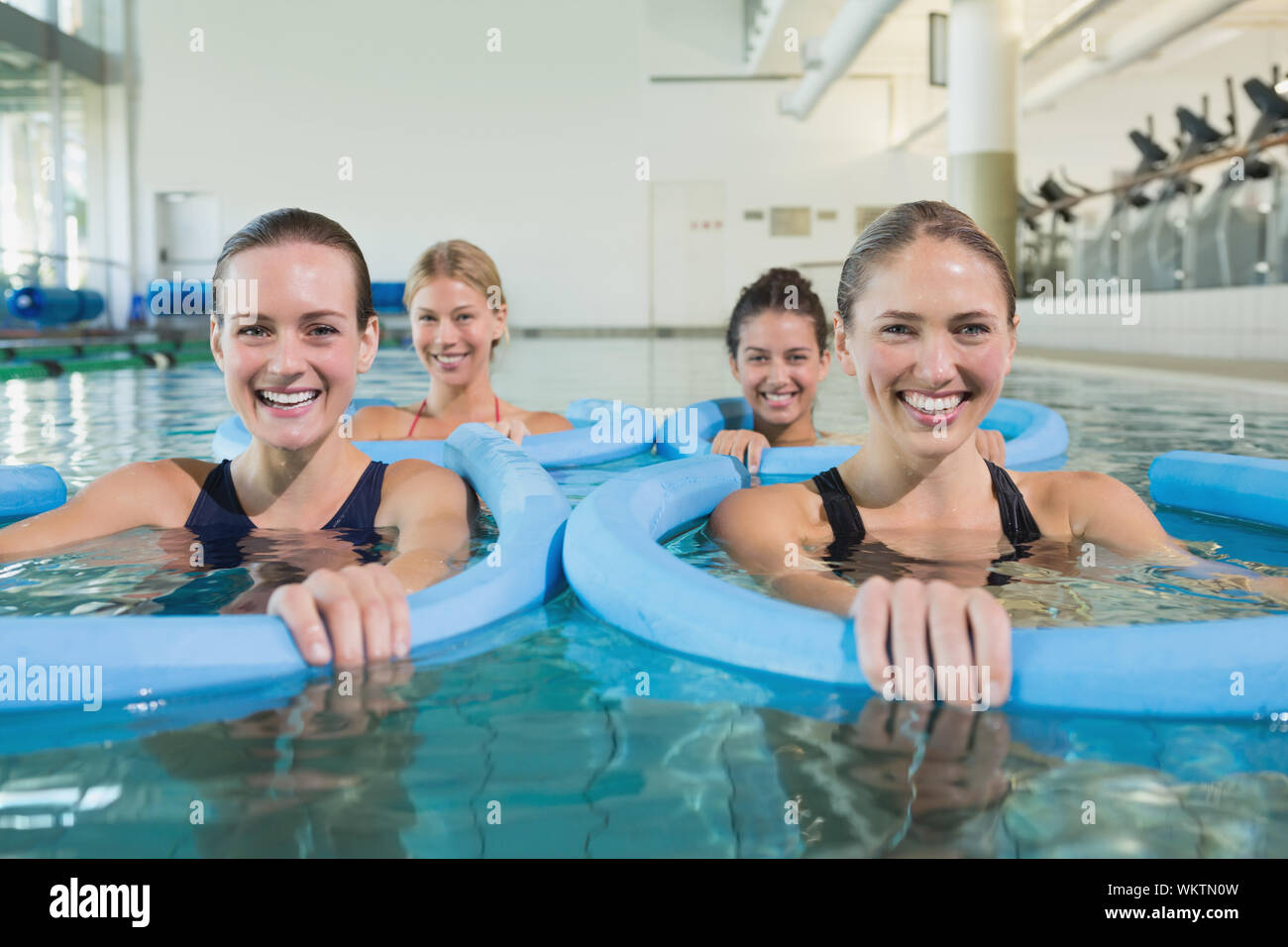 Happy fitness class doing aqua aerobics with foam rollers in swimming ...