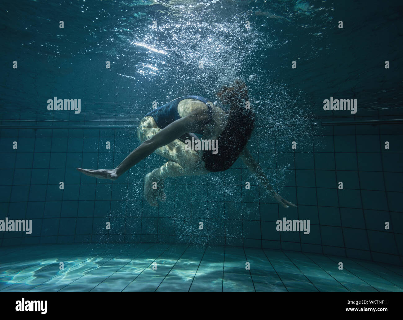 Athletic swimmer doing a somersault underwater in the swimming pool at ...