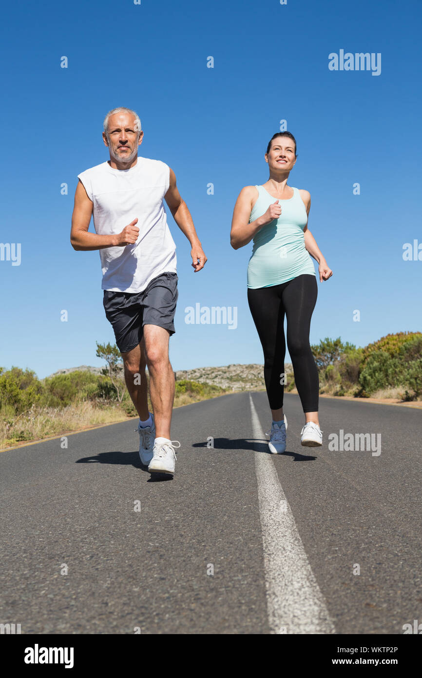 Fit couple running on the open road together on a sunny day Stock Photo ...
