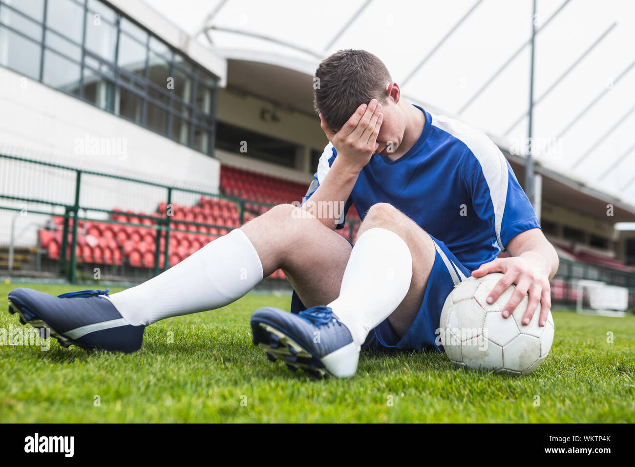 Disappointed football player in blue sitting on pitch after losing on a ...