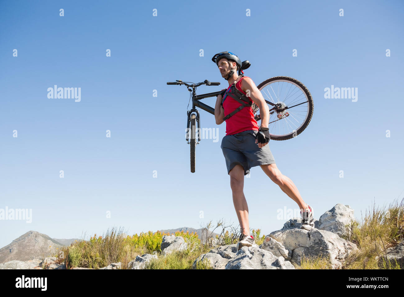 Fit cyclist carrying his bike on rocky terrain on a sunny day Stock ...