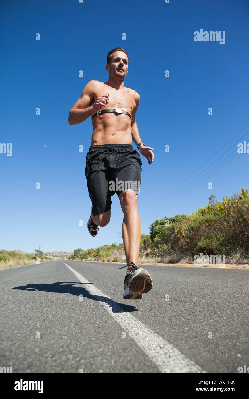 Athletic man jogging on open road with monitor around chest on a sunny day Stock Photo - Alamy