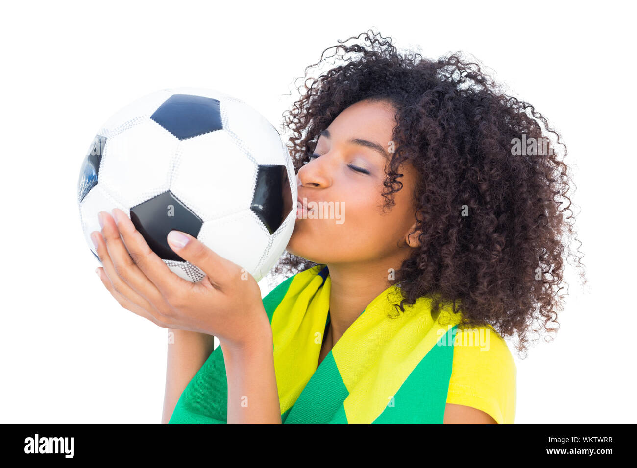 Pretty football fan with brazilian flag kissing ball on white ...