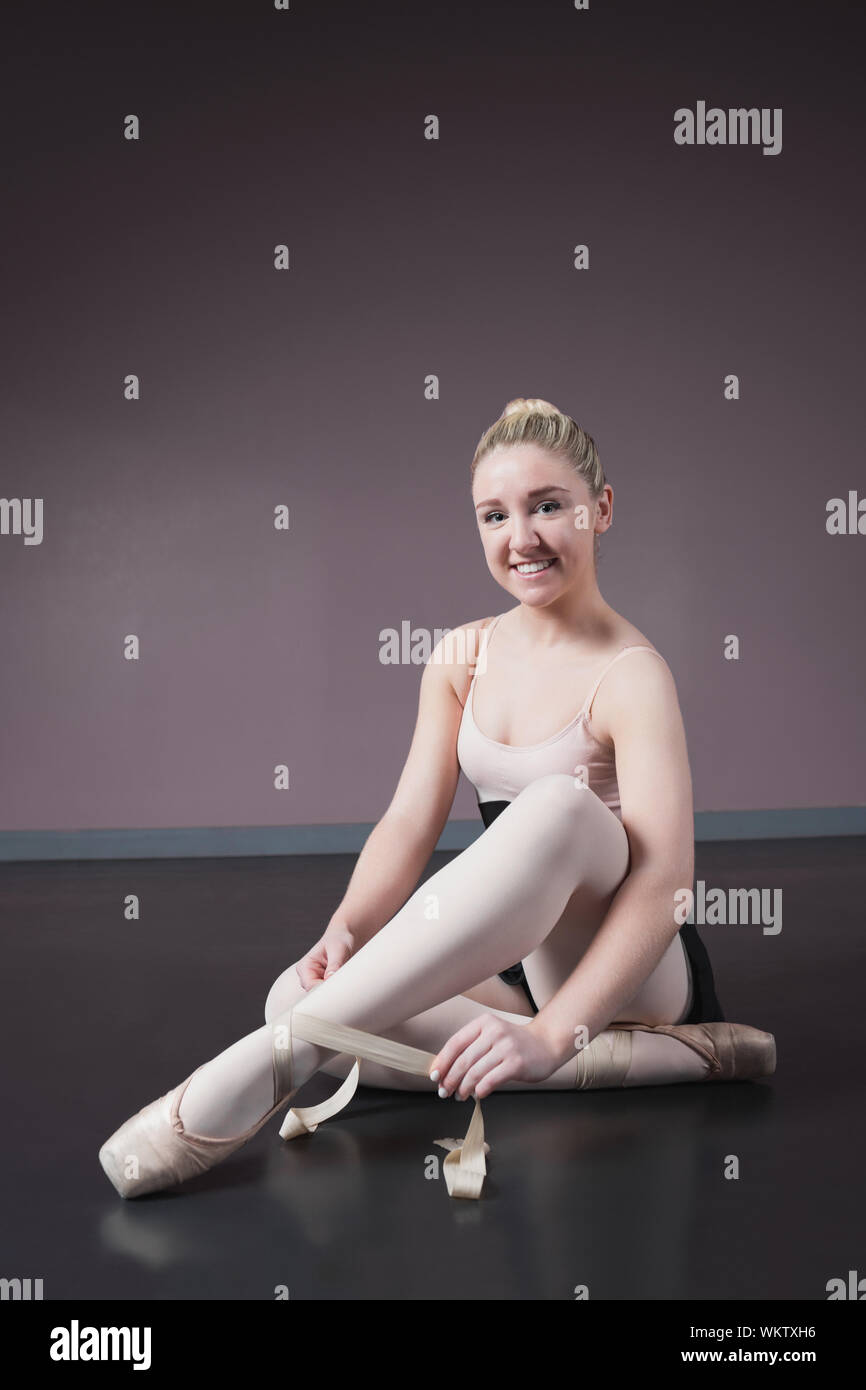 Pretty ballerina tying the ribbon on her ballet slippers in the ballet ...