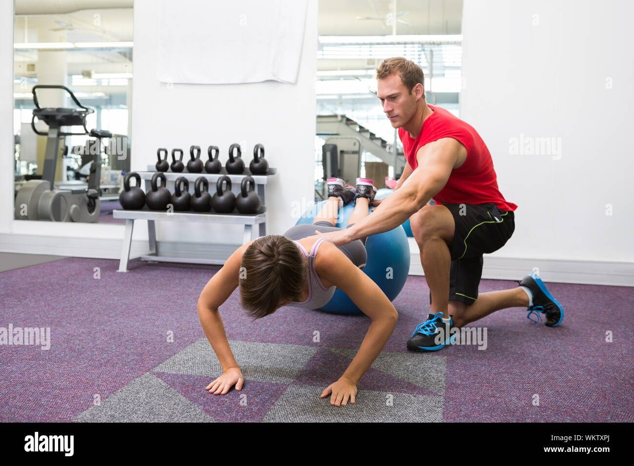 Personal trainer with client doing push up on exercise ball at the gym ...