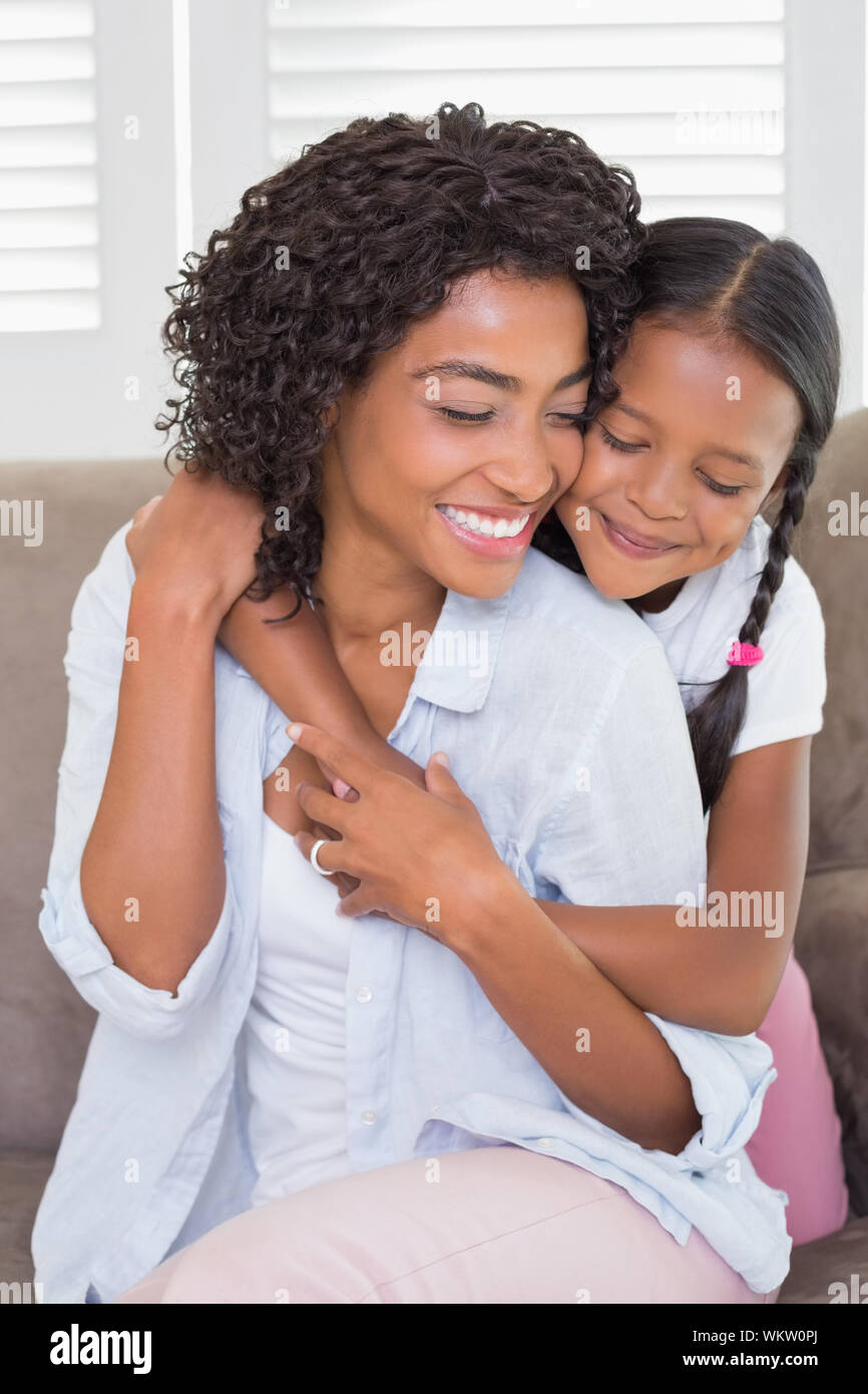 Pretty mother sitting on the couch with her daughter hugging at home in the living room Stock ...