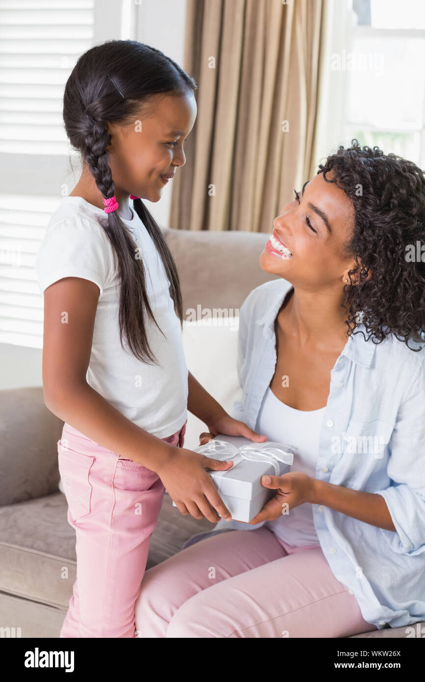 Pretty mother sitting on couch offering daughter a gift at home in the ...