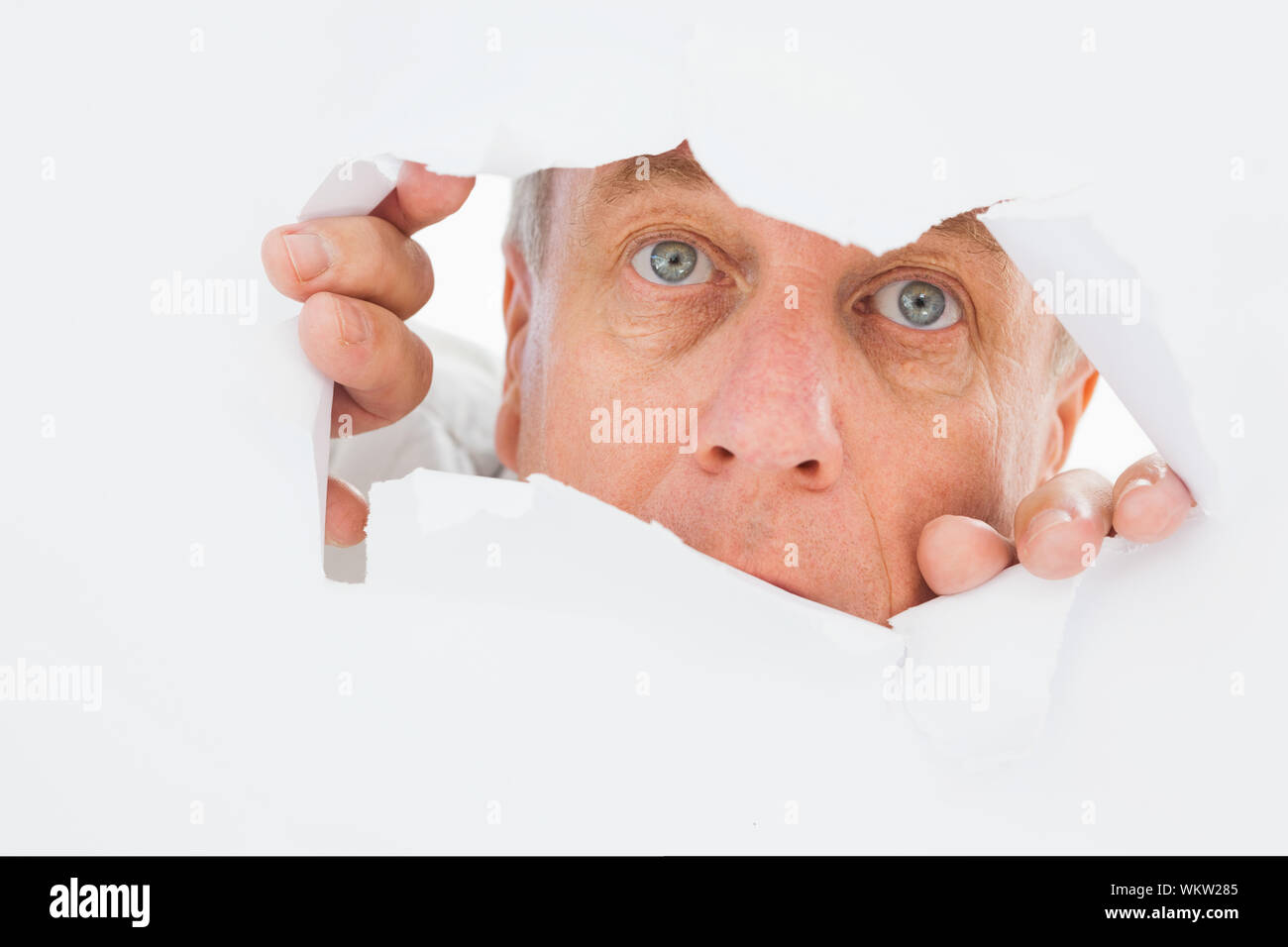 Older man looking through rip on white background Stock Photo - Alamy