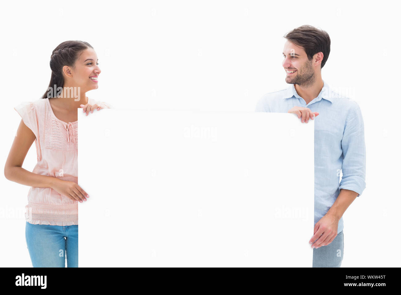 Attractive young couple smiling and holding poster on white background ...