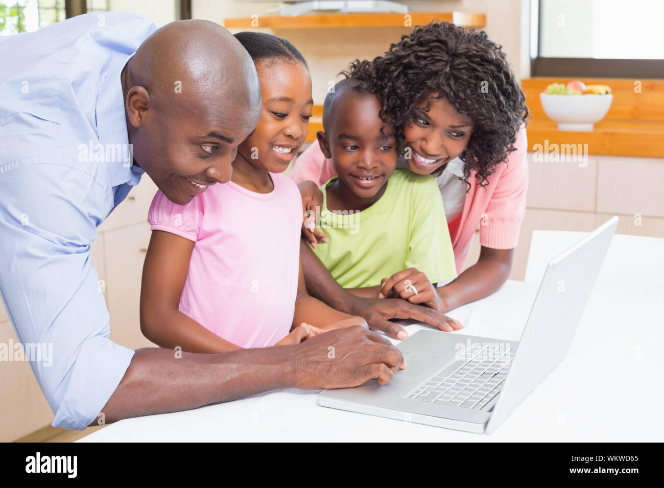 Cute siblings using laptop together with parents at home in the kitchen ...