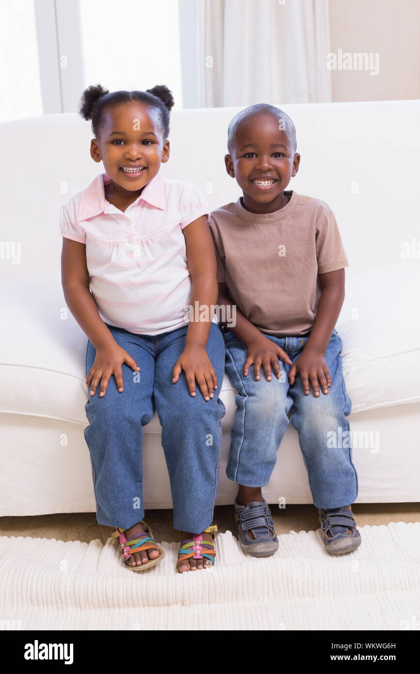 Happy siblings smiling at camera together at home in the living room ...