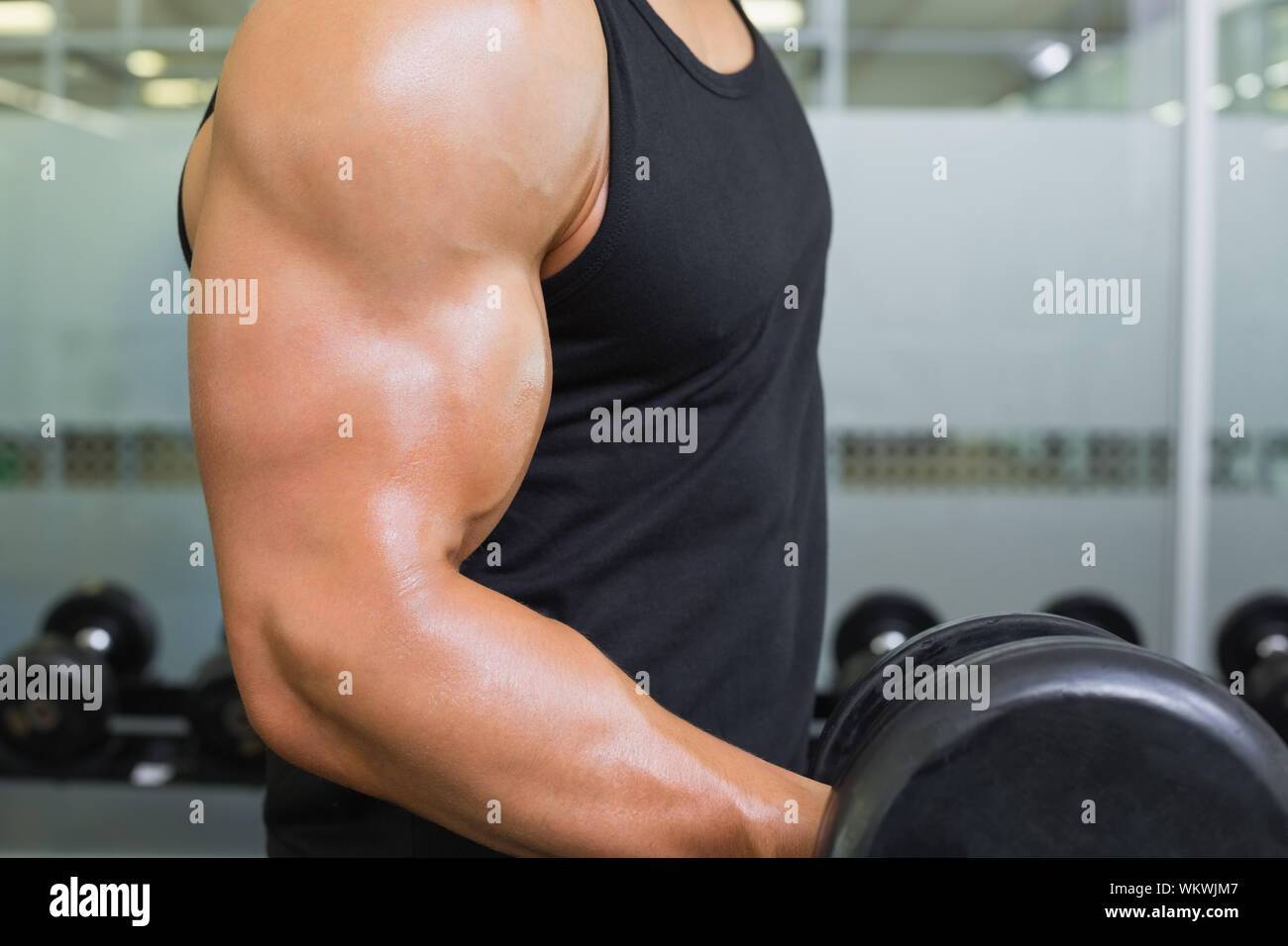 Side view of a young muscular man exercising with dumbbell in gym Stock ...