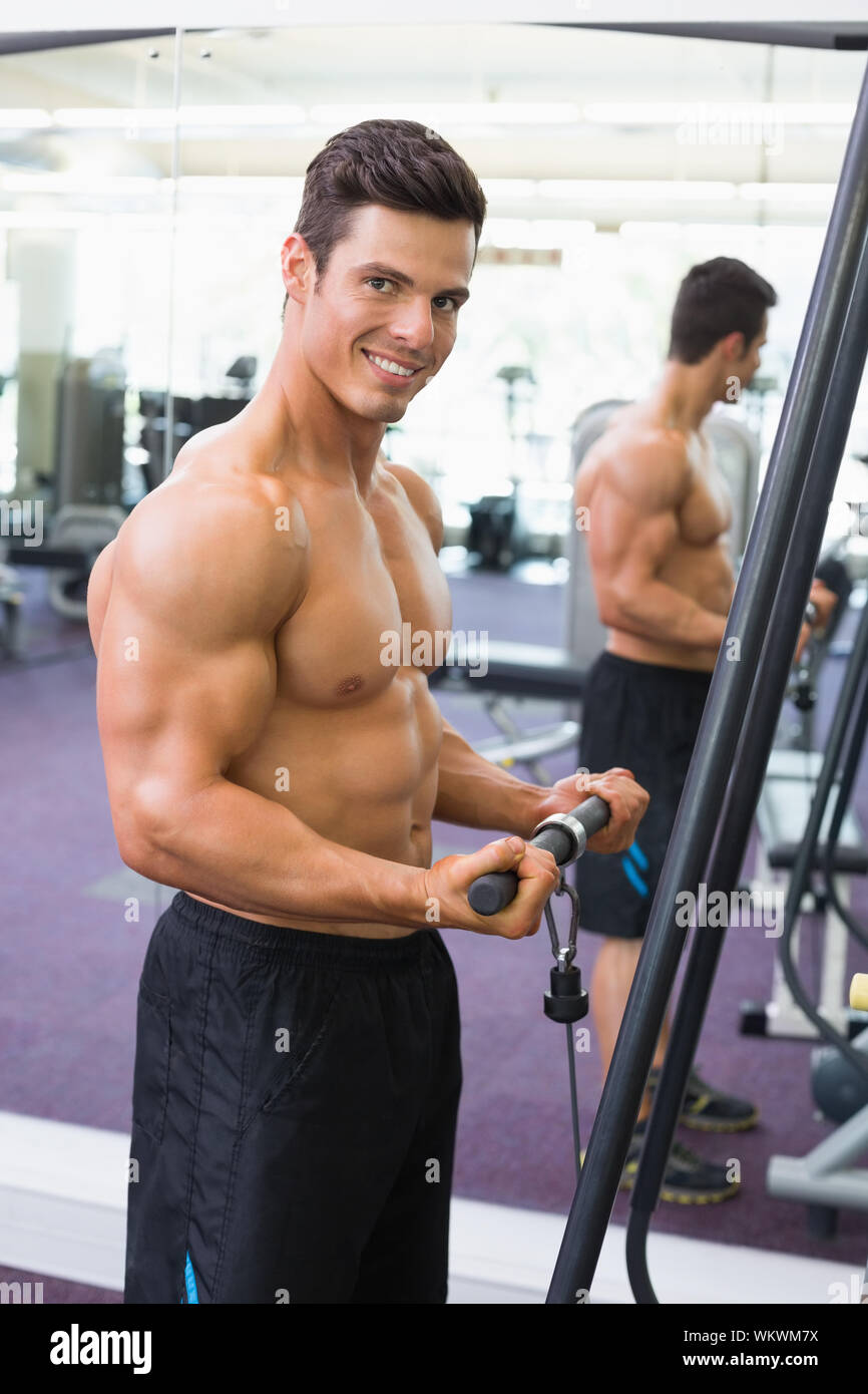 Side view portrait of a shirtless young muscular man using triceps pull ...