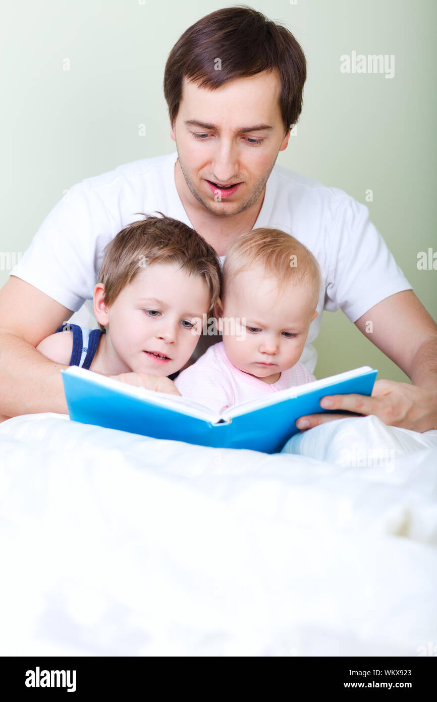 Young father and two kids reading book in bed Stock Photo - Alamy